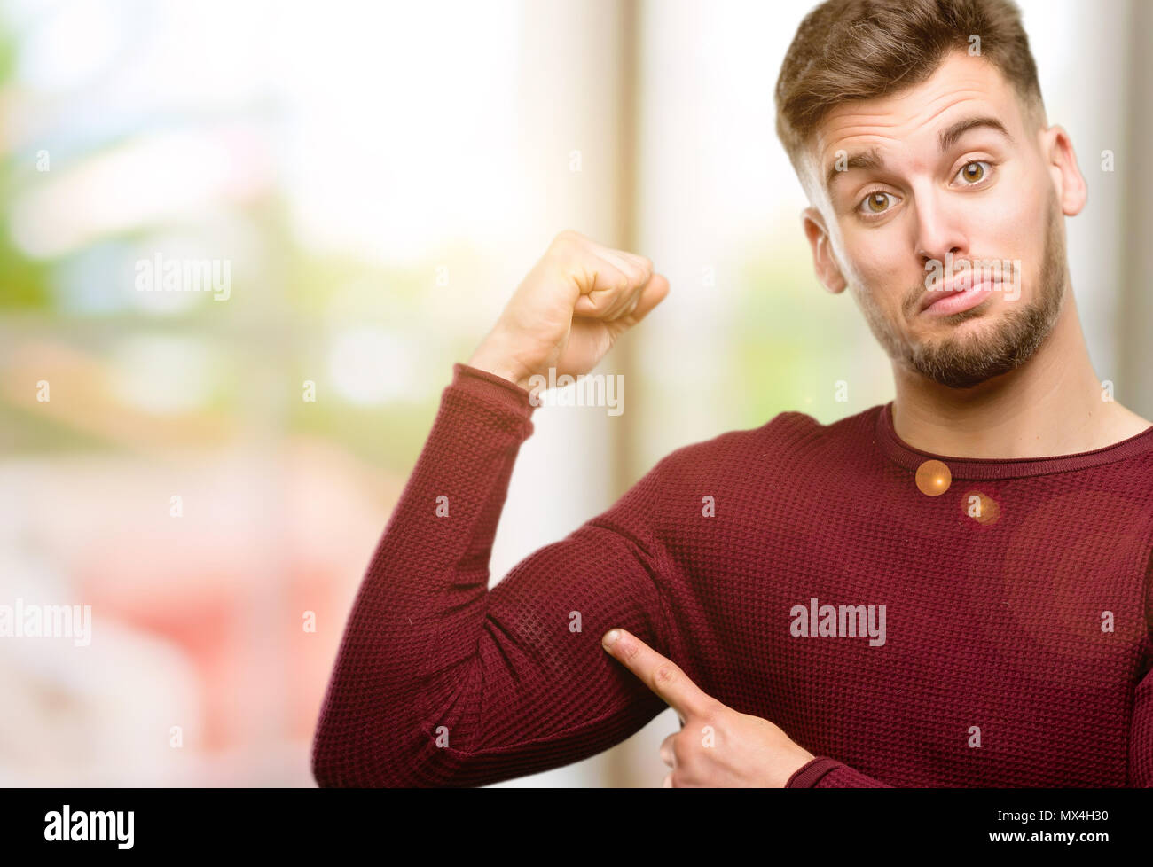Handsome young man pointing biceps expressing strength and gym concept ...
