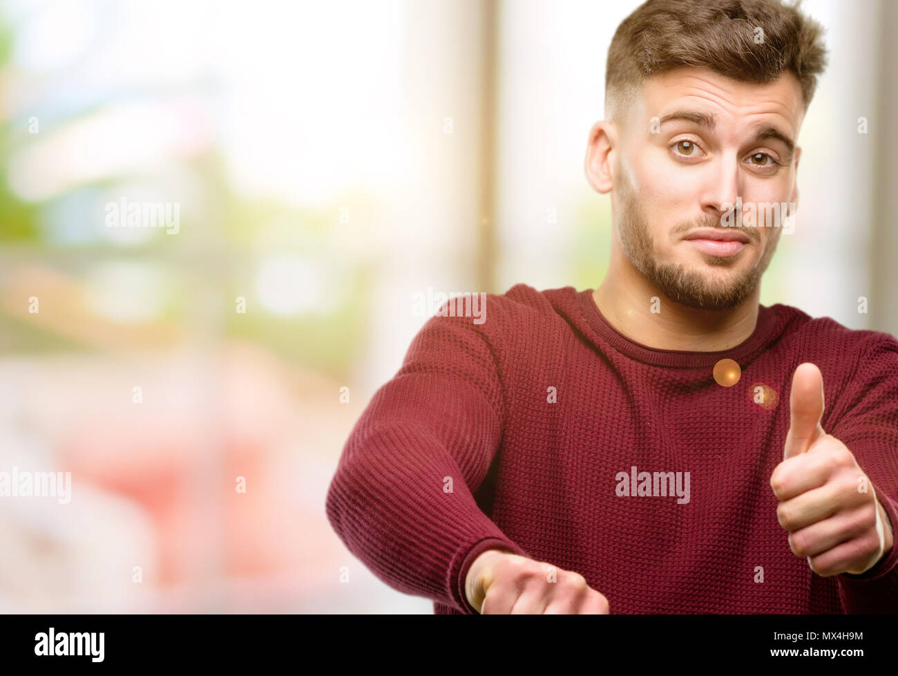 Handsome young man confused with thumbs up and down, trying to take a ...