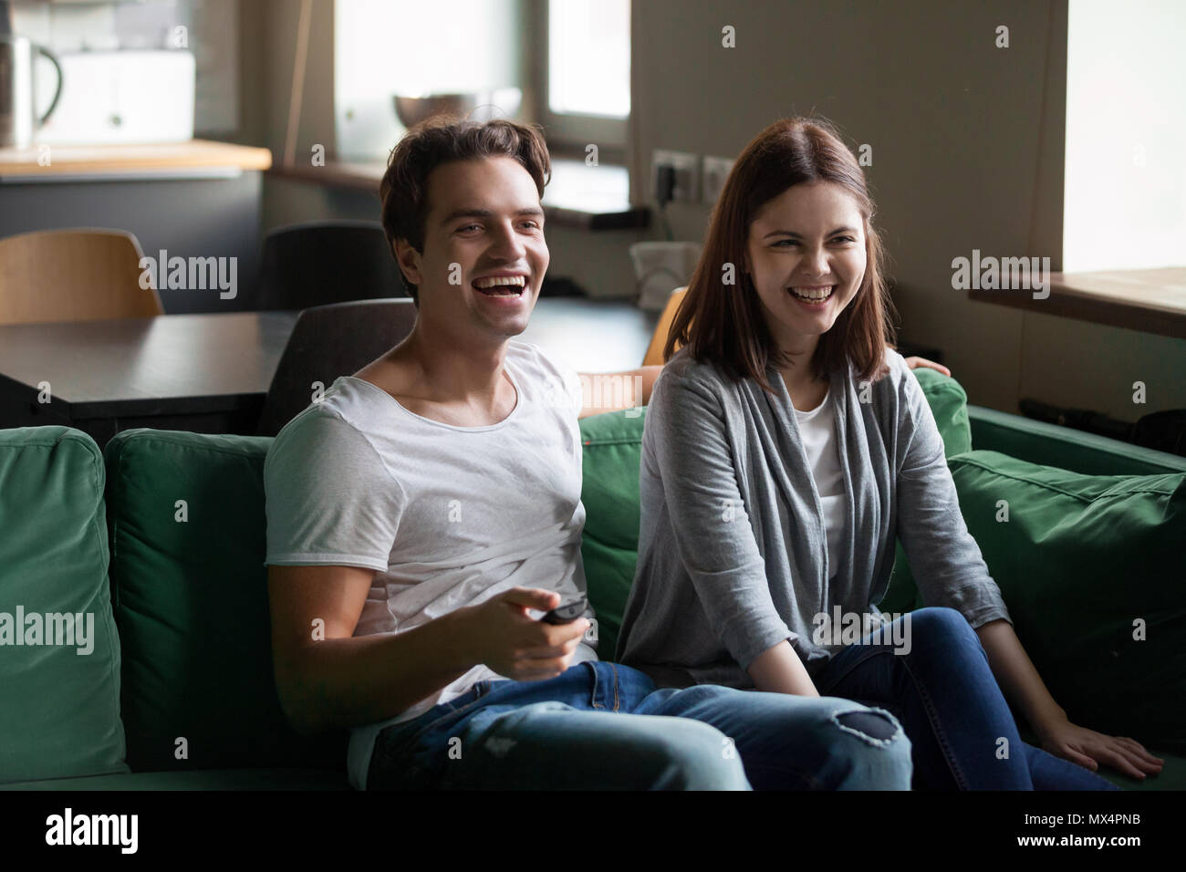 Millennial couple laughing watching tv holding remote control at Stock ...