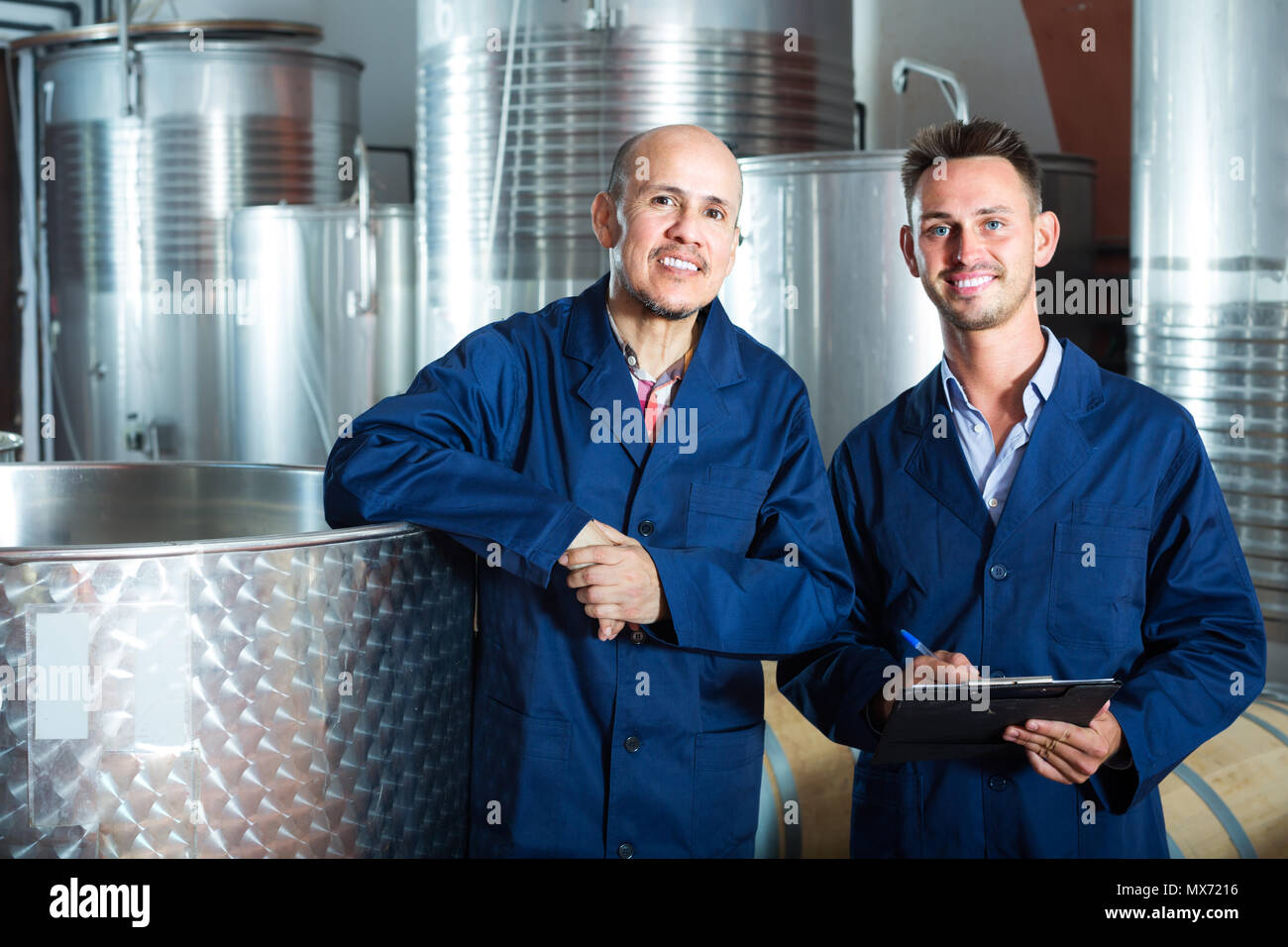 Two male winery employees working and taking notes in secondary ...