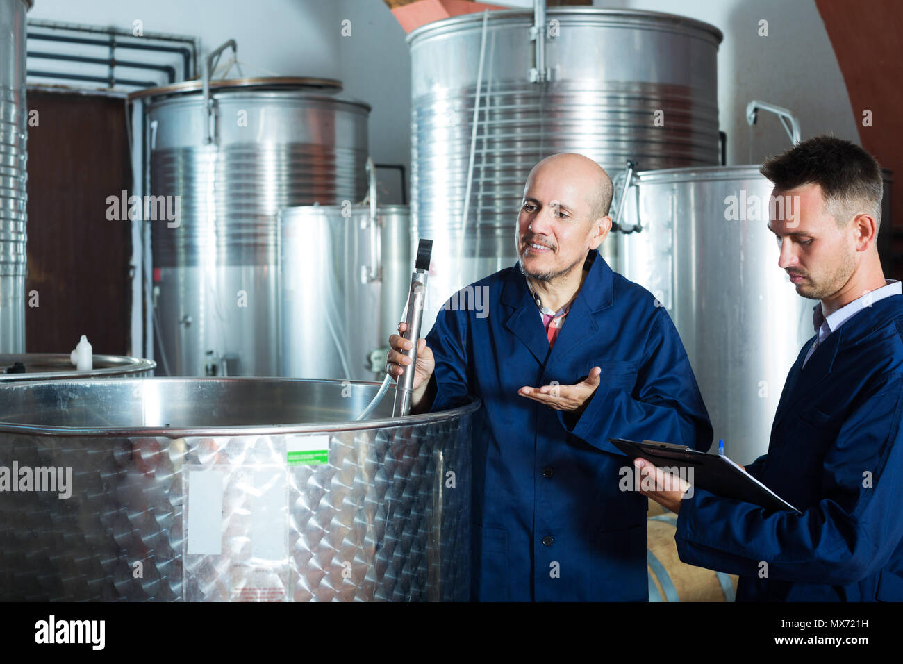 Positive winery workers taking notes while checking equipment in ...