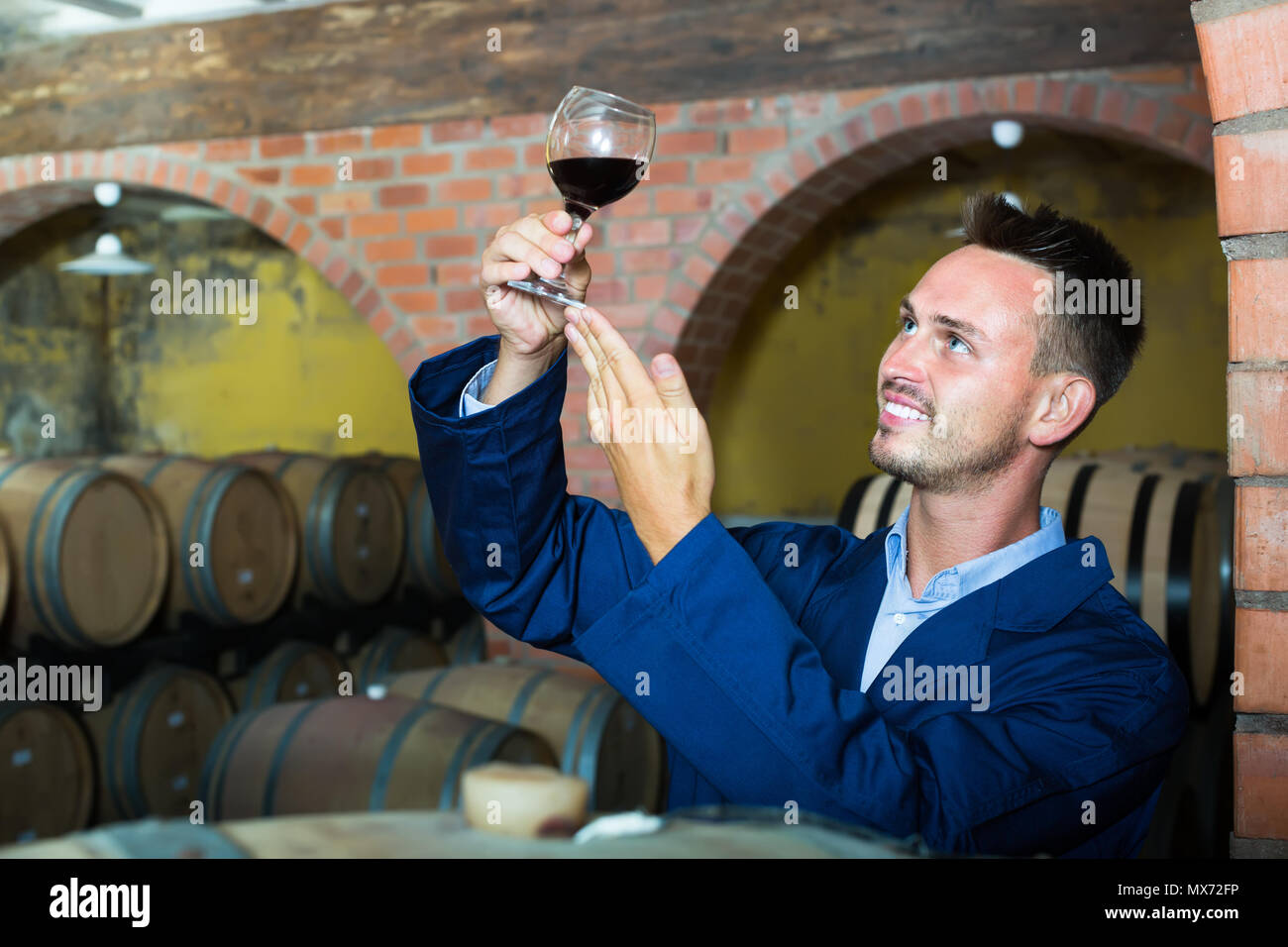 Young smiling winery worker wearing coat holding glass of wine in ...