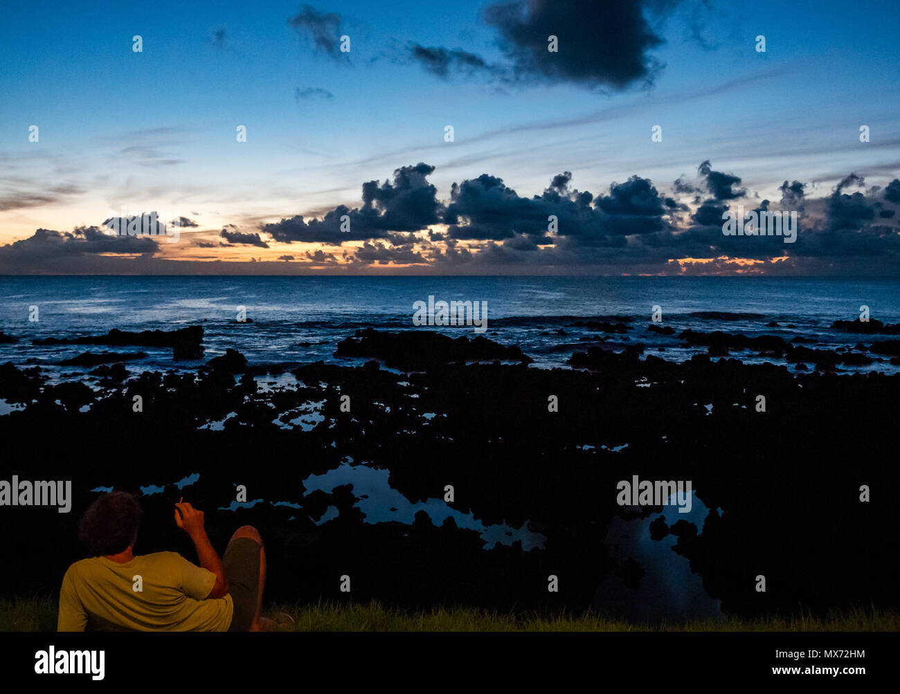 Man relaxing sitting on ground smoking, watching the sunset, Hanga Roa ...