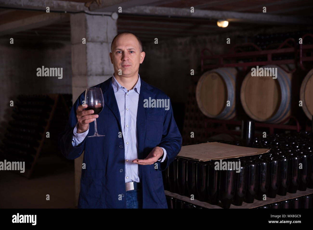 Confident winemaker inviting to wine cellar, offering glass of red wine ... Confident winemaker inviting to wine cellar, offering glass of red wine ...