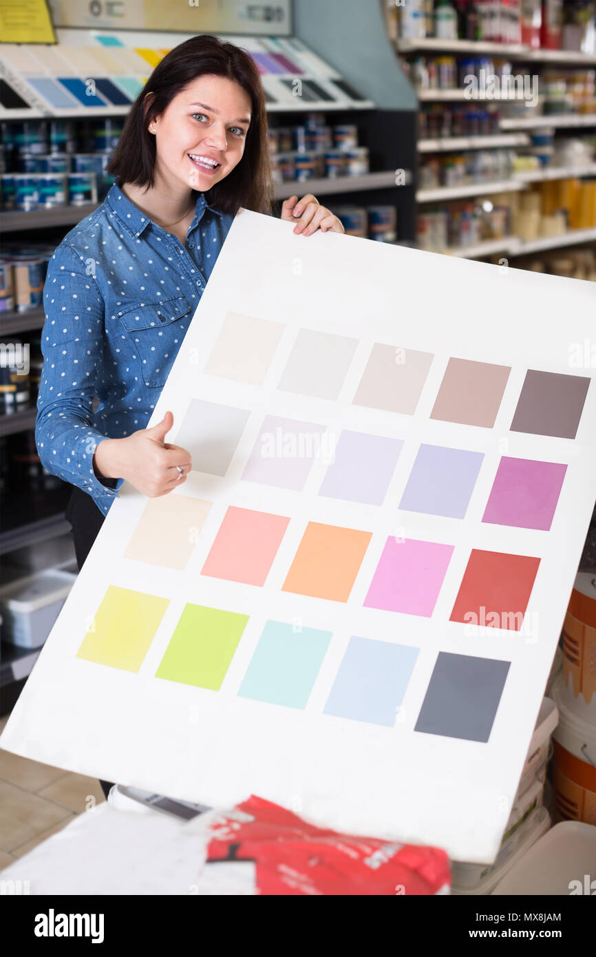happy female customer examining color scheme variants in paint supplies ...