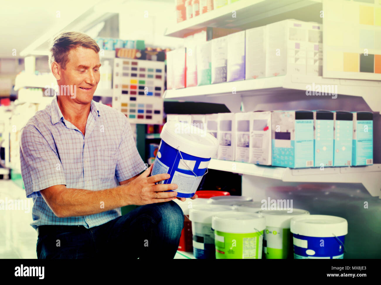 Portrait of cheerful positive smiling male customer selecting paint can ...
