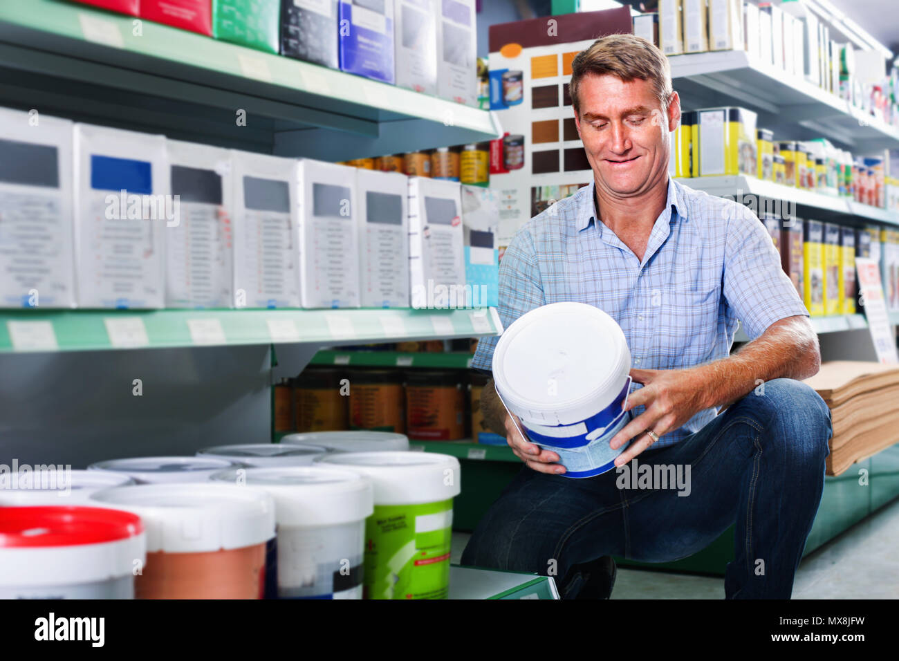 Portrait of positive smiling male customer selecting paint can in ...