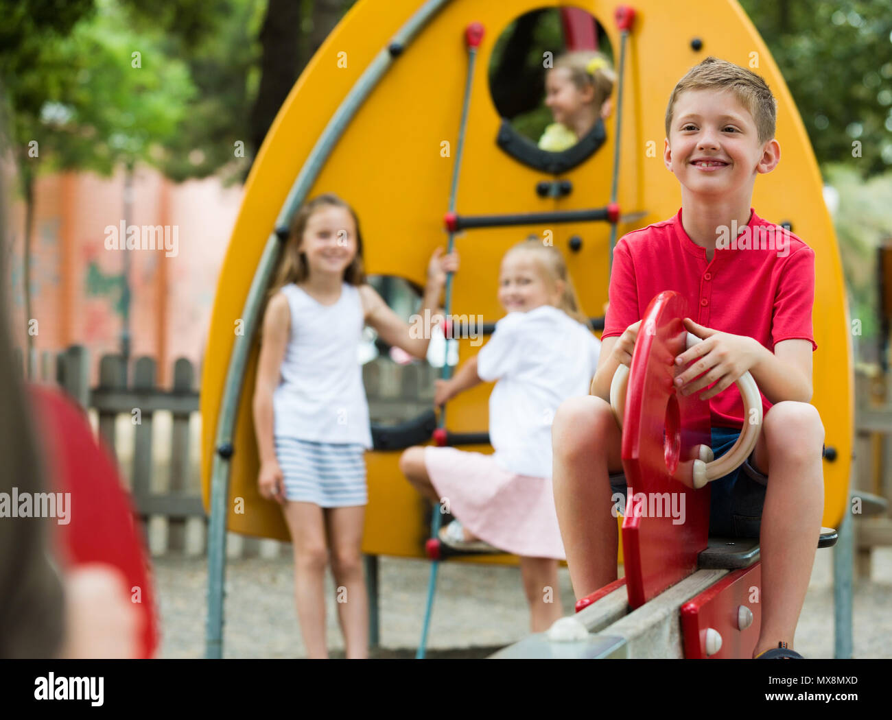 portrait of glad boy sitting on swinging toy while other children ...