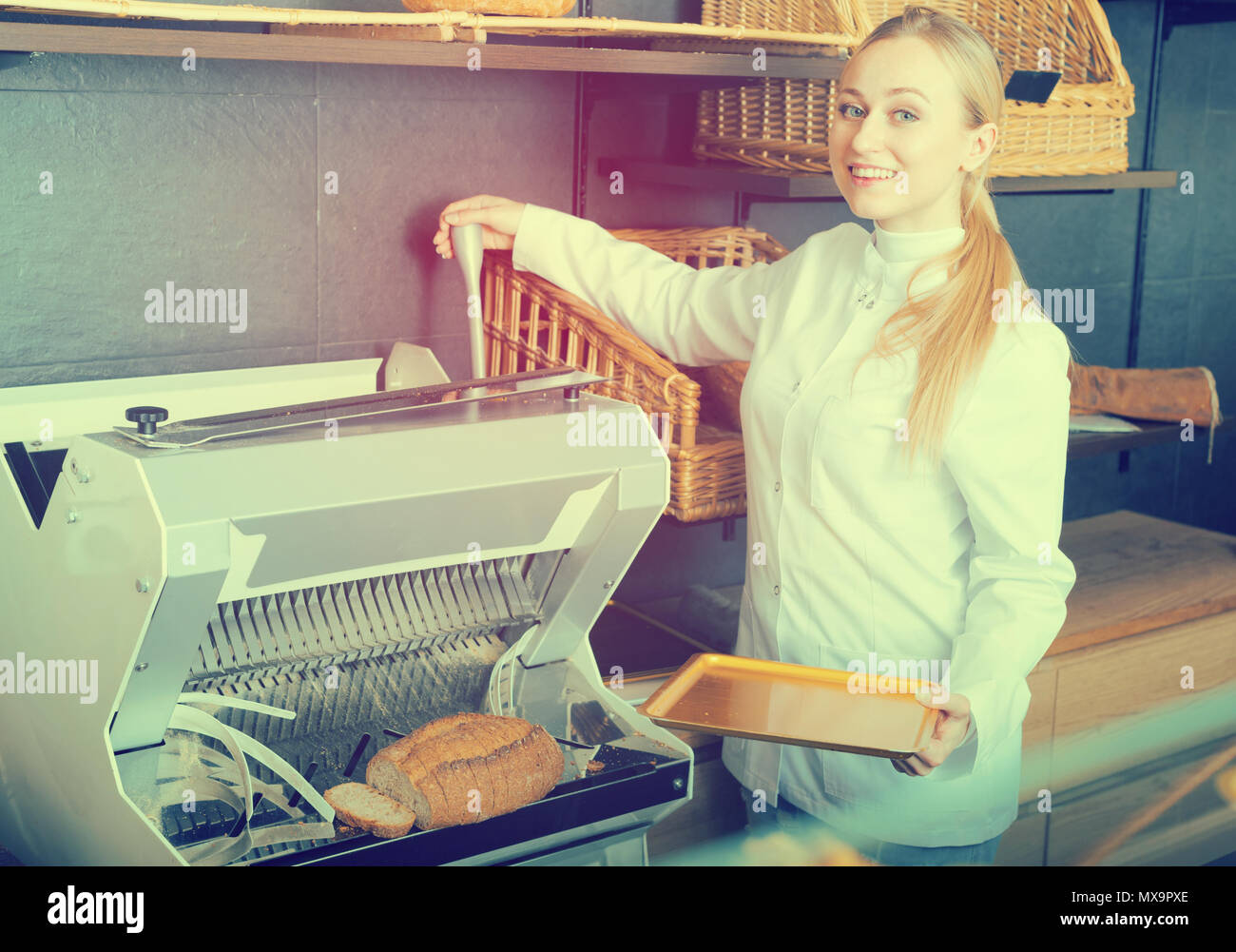 Happy young girl dressed as baker showing automatically cut bread in ...