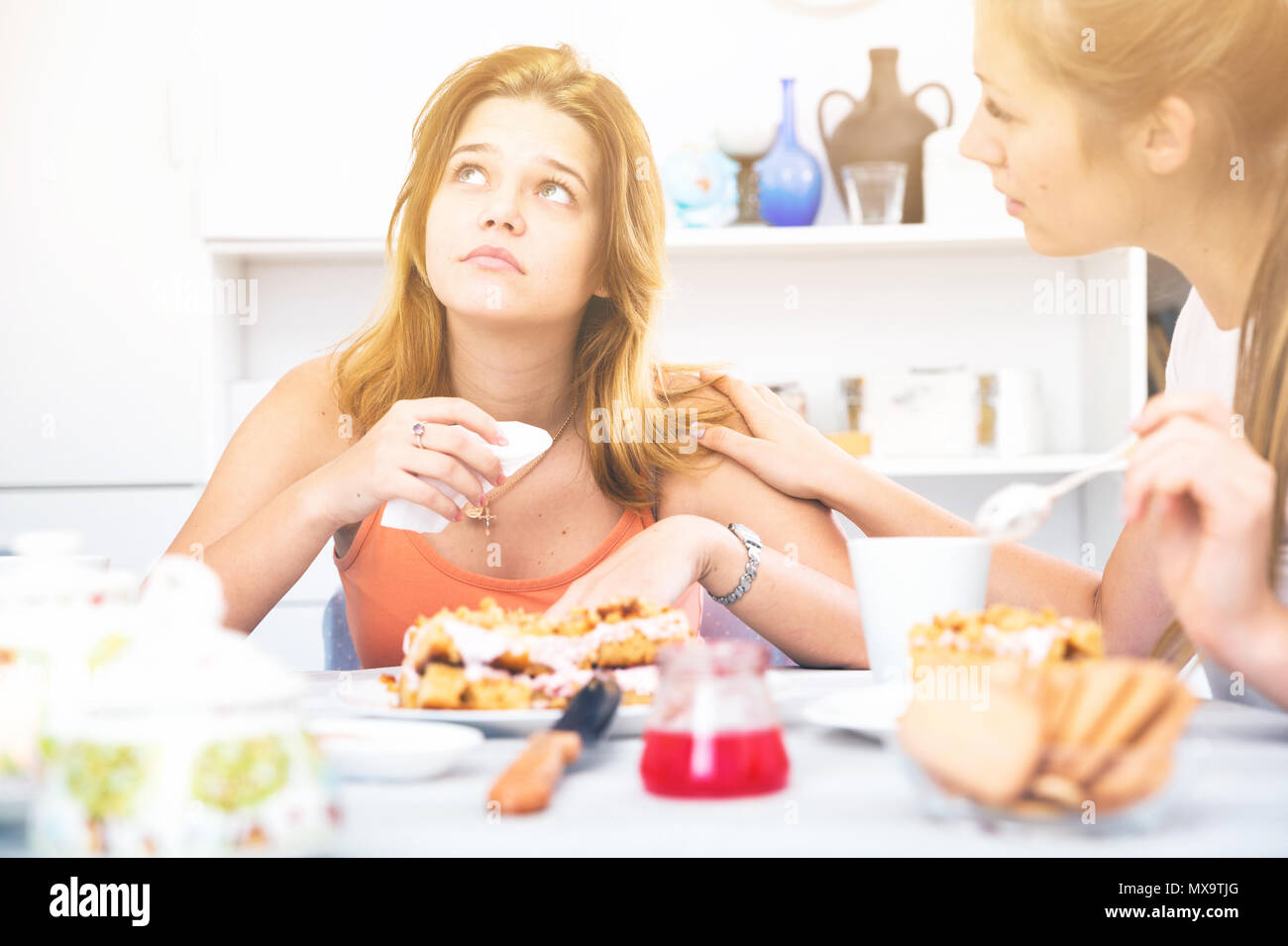 Female talking with young sad friend at the table with cake at home ...