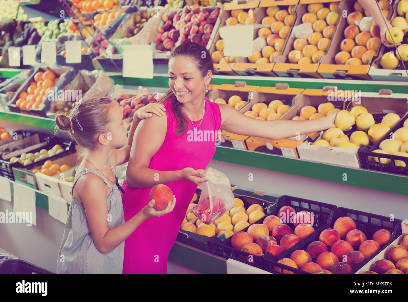Portrait of smiling mother with girl taking peaches at fruit market ...