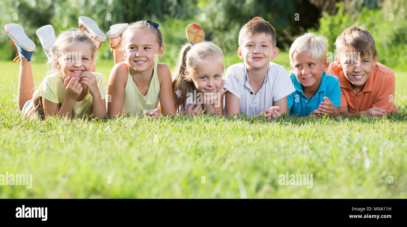 Group of glad kids in elementary school age lying on green grass in ...