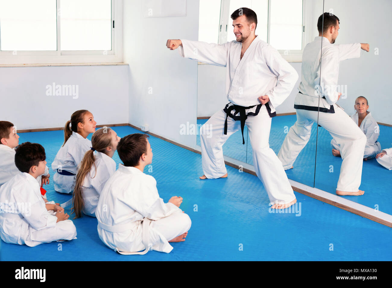 Smiling cheerful positive coach showing new martial moves to children ...