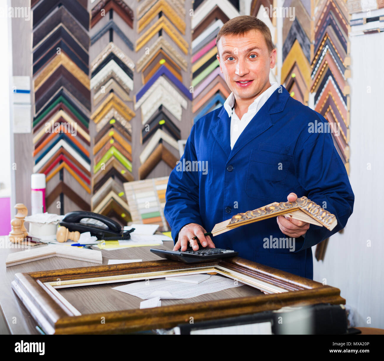 Cheerful diligent man worker holding picture frame details on counter ...