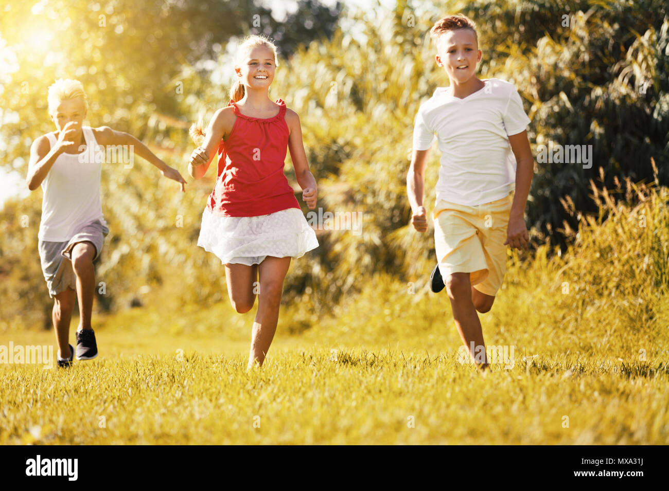 Three happy adult kids playing active games in summer park chasing each ...