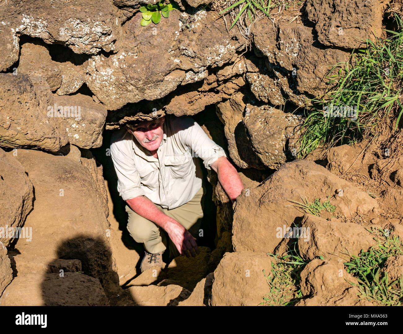 Senior man climbing out of narrow opening of volcanic tube cave, Ana ...