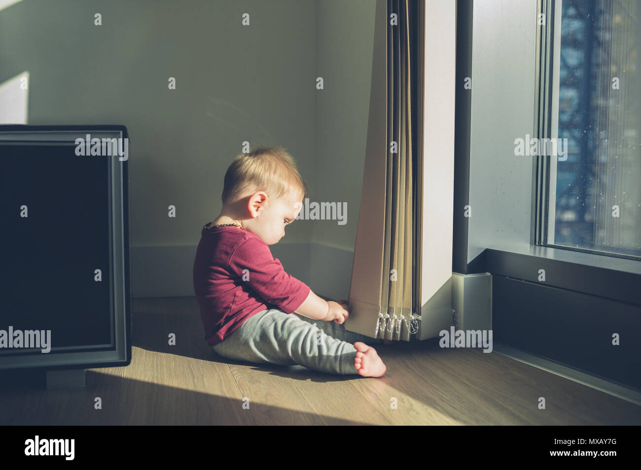 A little baby is sitting by the window in a high rise apartment Stock ...