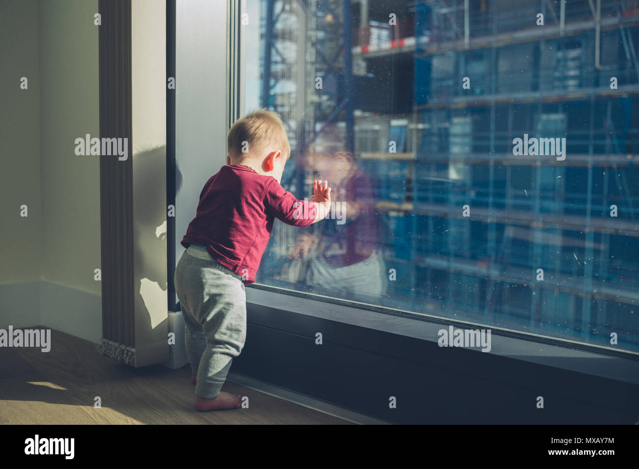 A little baby is standing by the window in a high rise apartment Stock ...