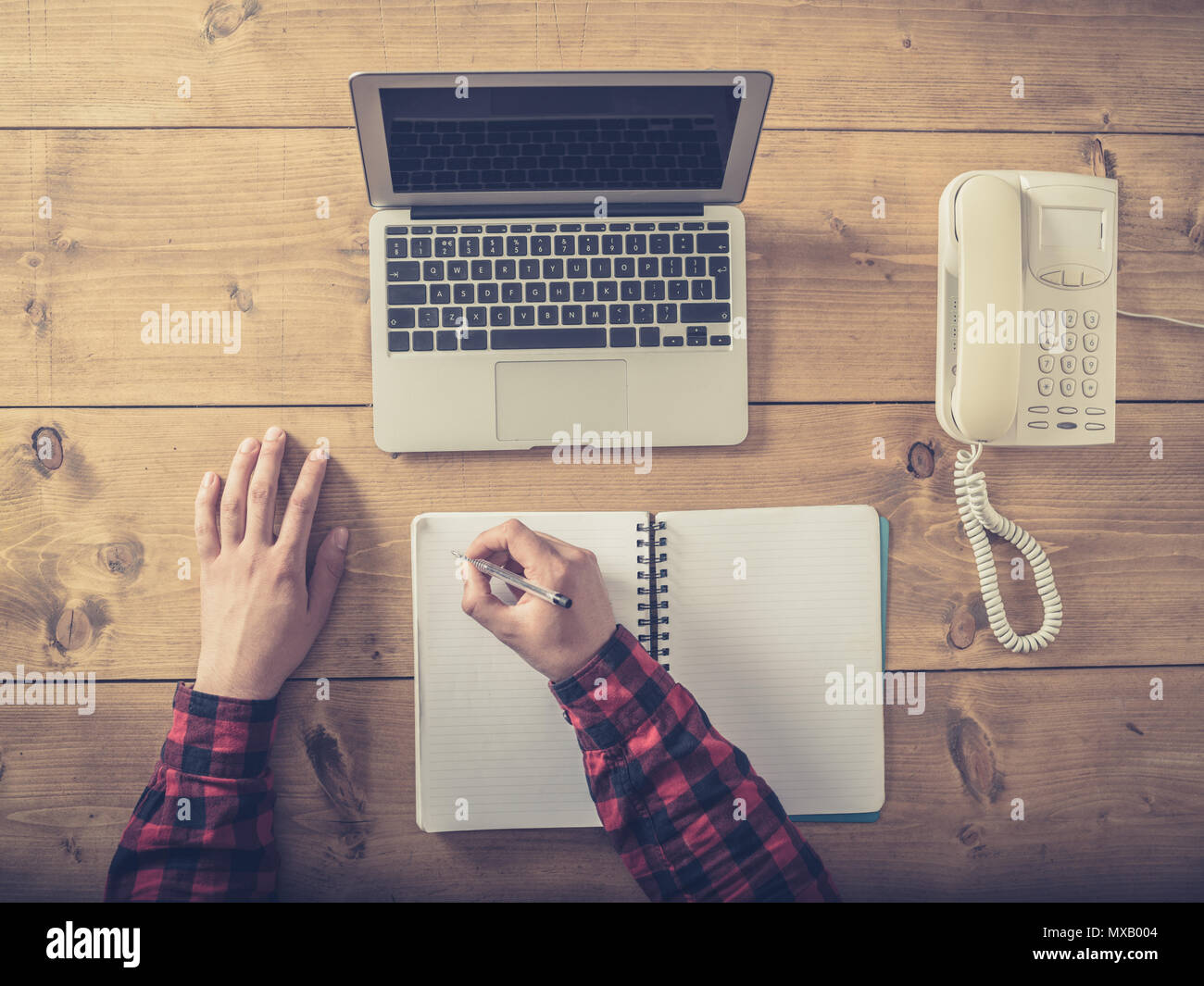 Overhead shot of a man at a desk using a laptop and writing in a ...