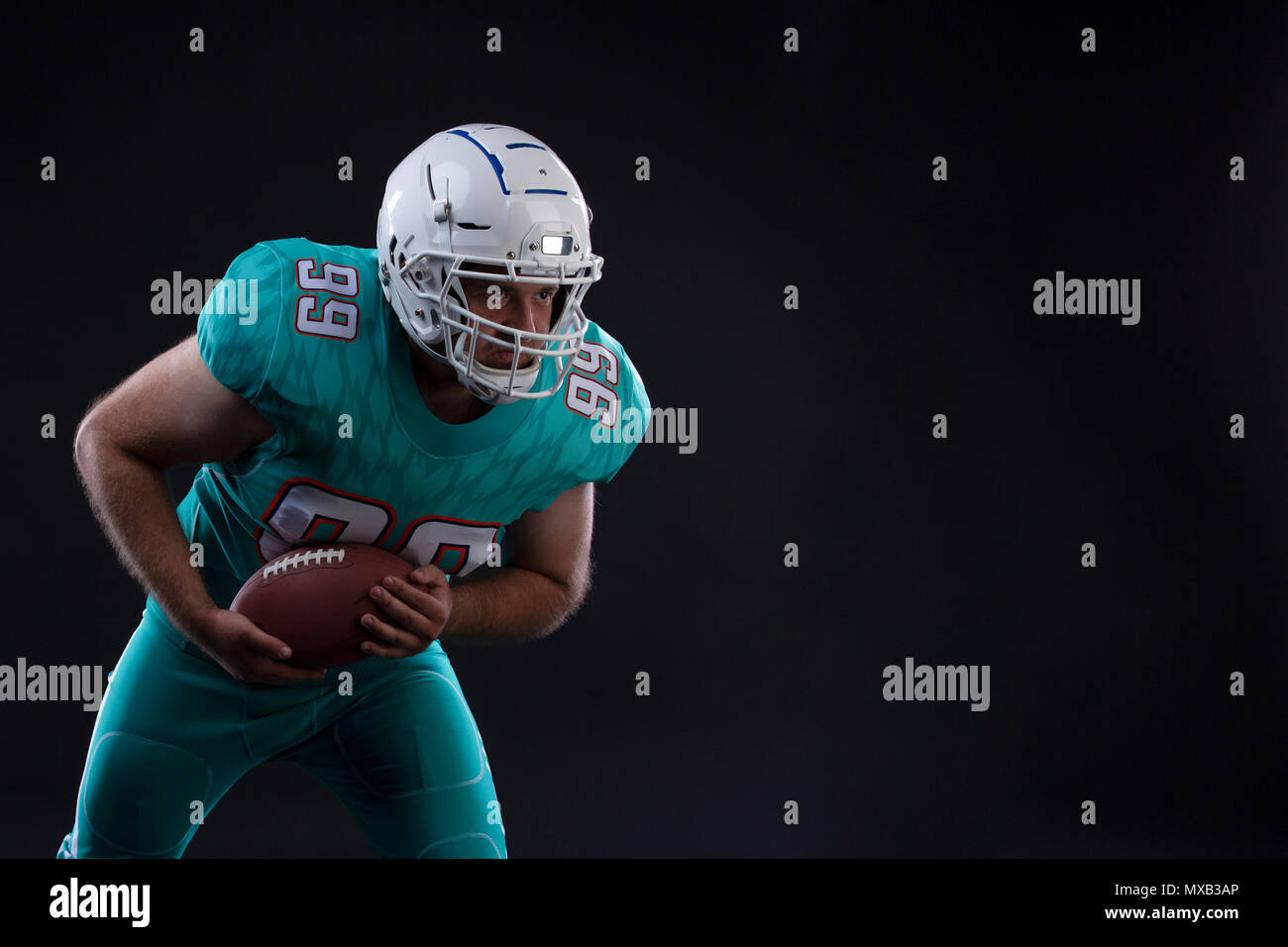 Portrait of American football player holding a ball in both his arms on ...