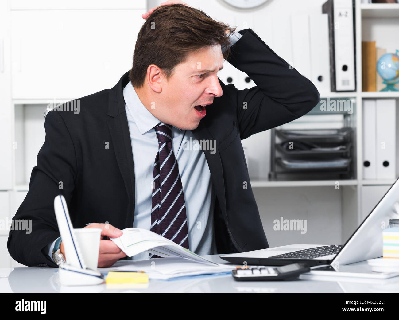 Busy businessman in suit worrying at the computer with cup of water ...