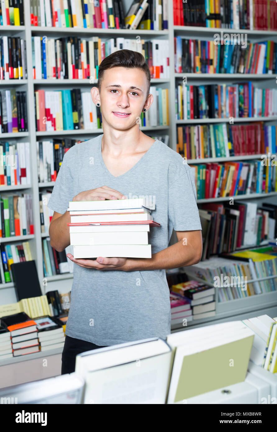 joyful teenage boy holding book pile in hands in book shop Stock Photo ...