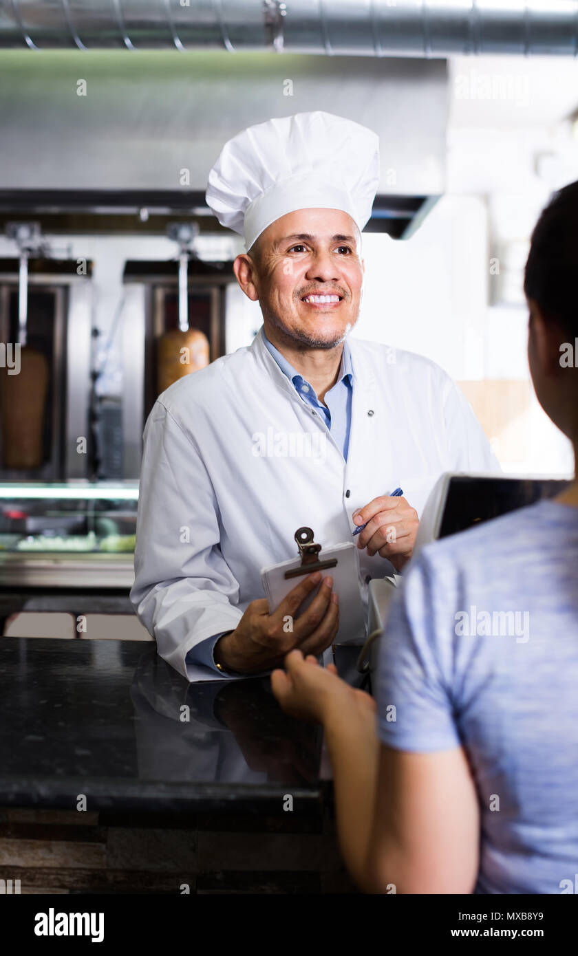 cheerful mature man cook taking order from customer on counter in fast ...