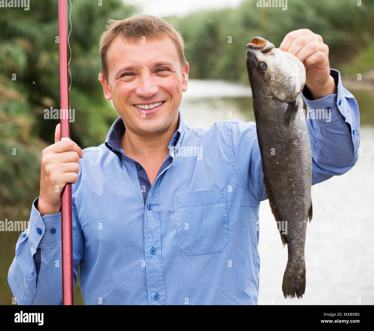 Glad man holding a fish after fishing on a river side Stock Photo - Alamy