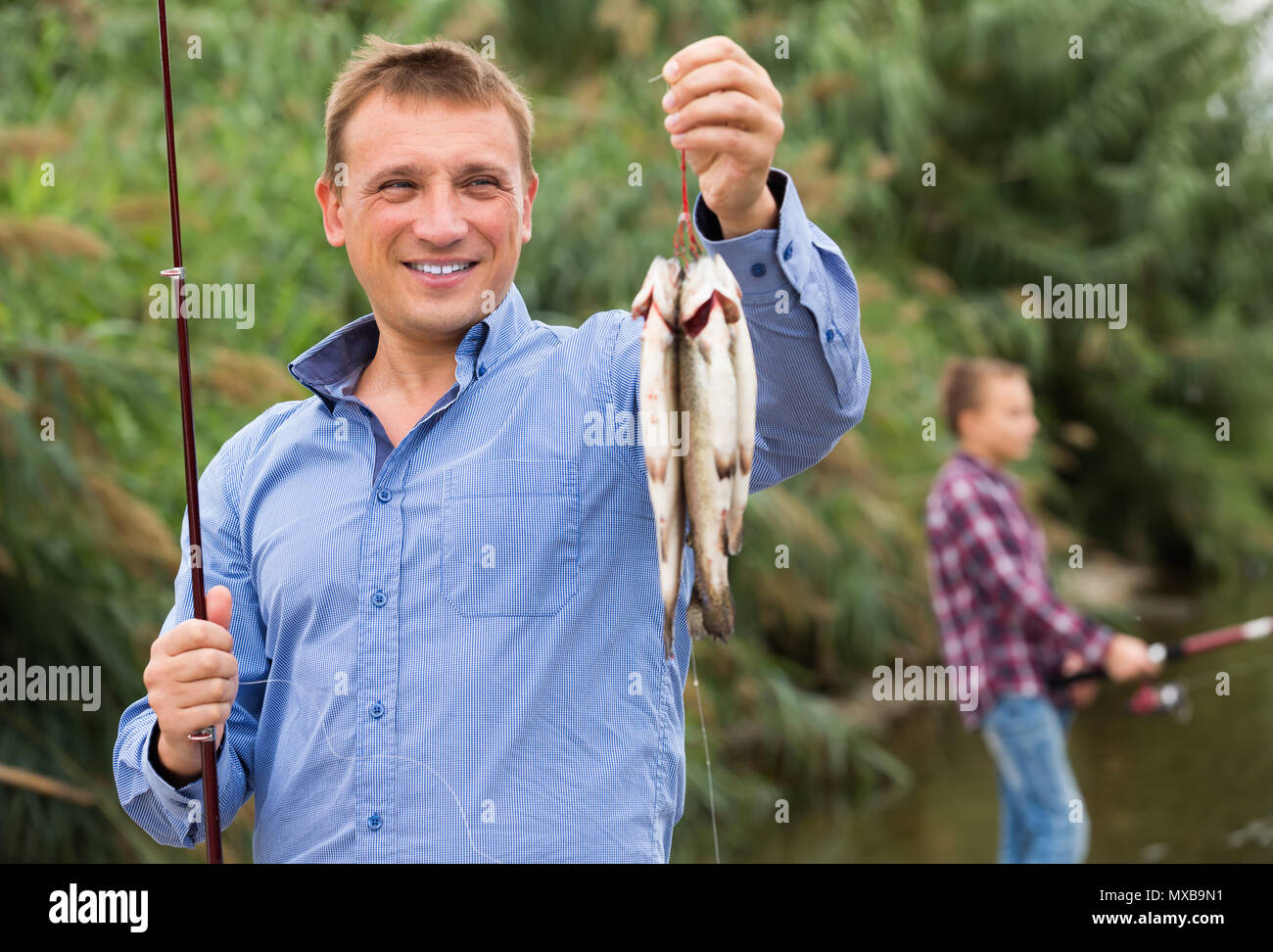 Positive fisherman holding catch freshwater fish in hands on river ...