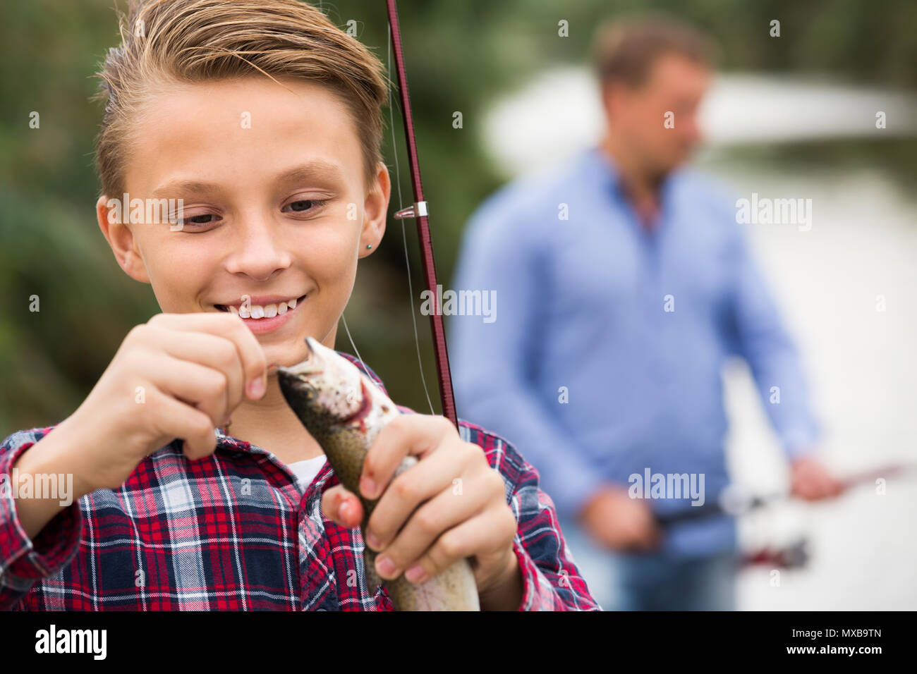 portrait of cheerful teenager boy holding catch fish on hook outdoors ...