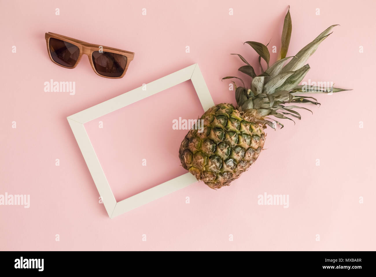 Flat lay of pineapple with sunglasses and empty picture frame against ...