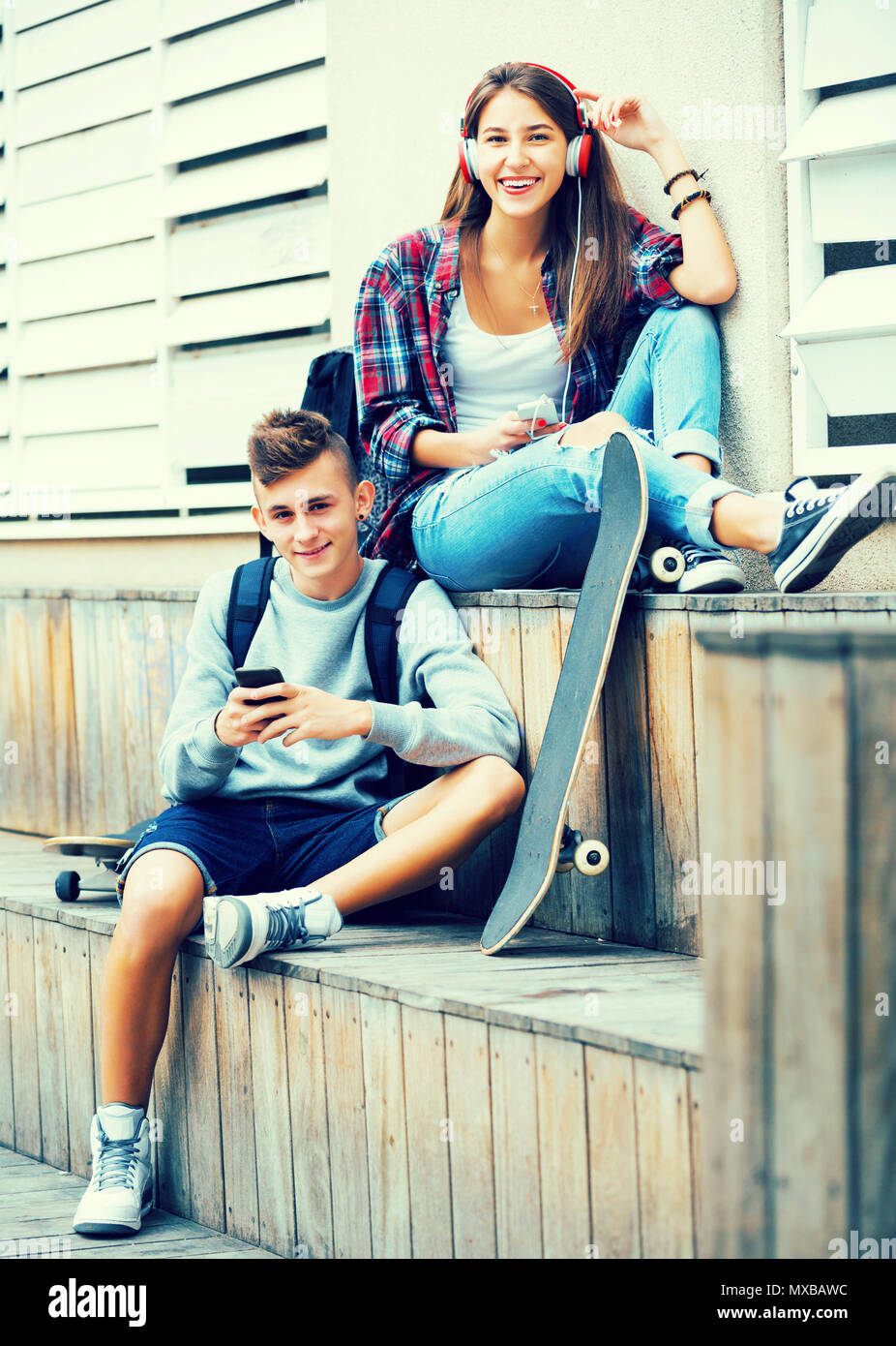Positive friends relaxing with mobile phones in sunny day outdoors ...
