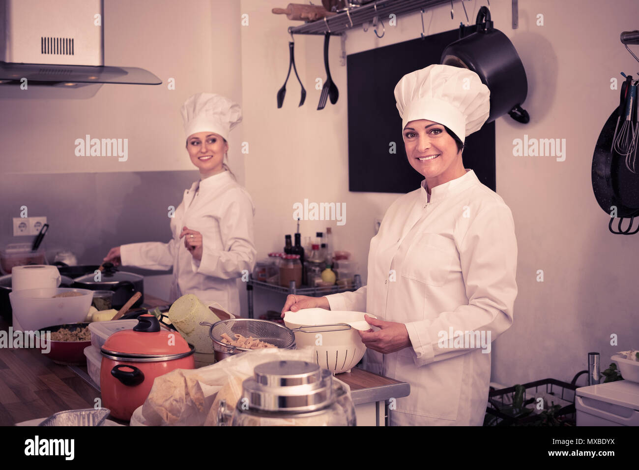 Cheerful charming female chefs preparing food on restaurant kitchen ...