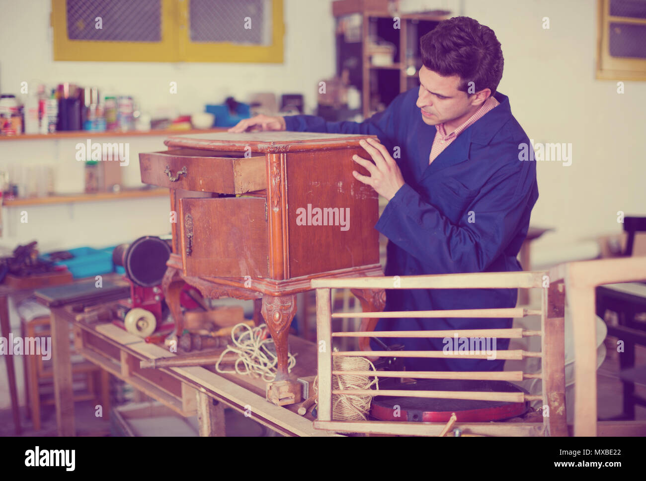 Man carpenter wearing blue overalls restoring furniture in restoration ...