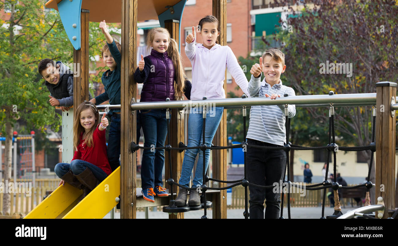 Smiling glad children in school age sliding down together on playground ...