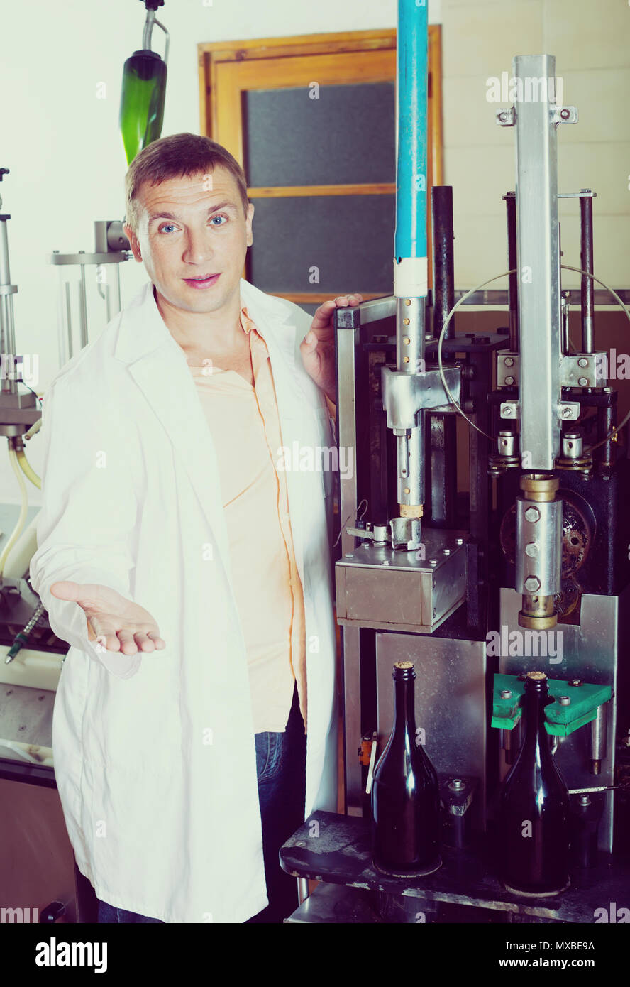 Male assembly line operator in white robe working in modern wine ...