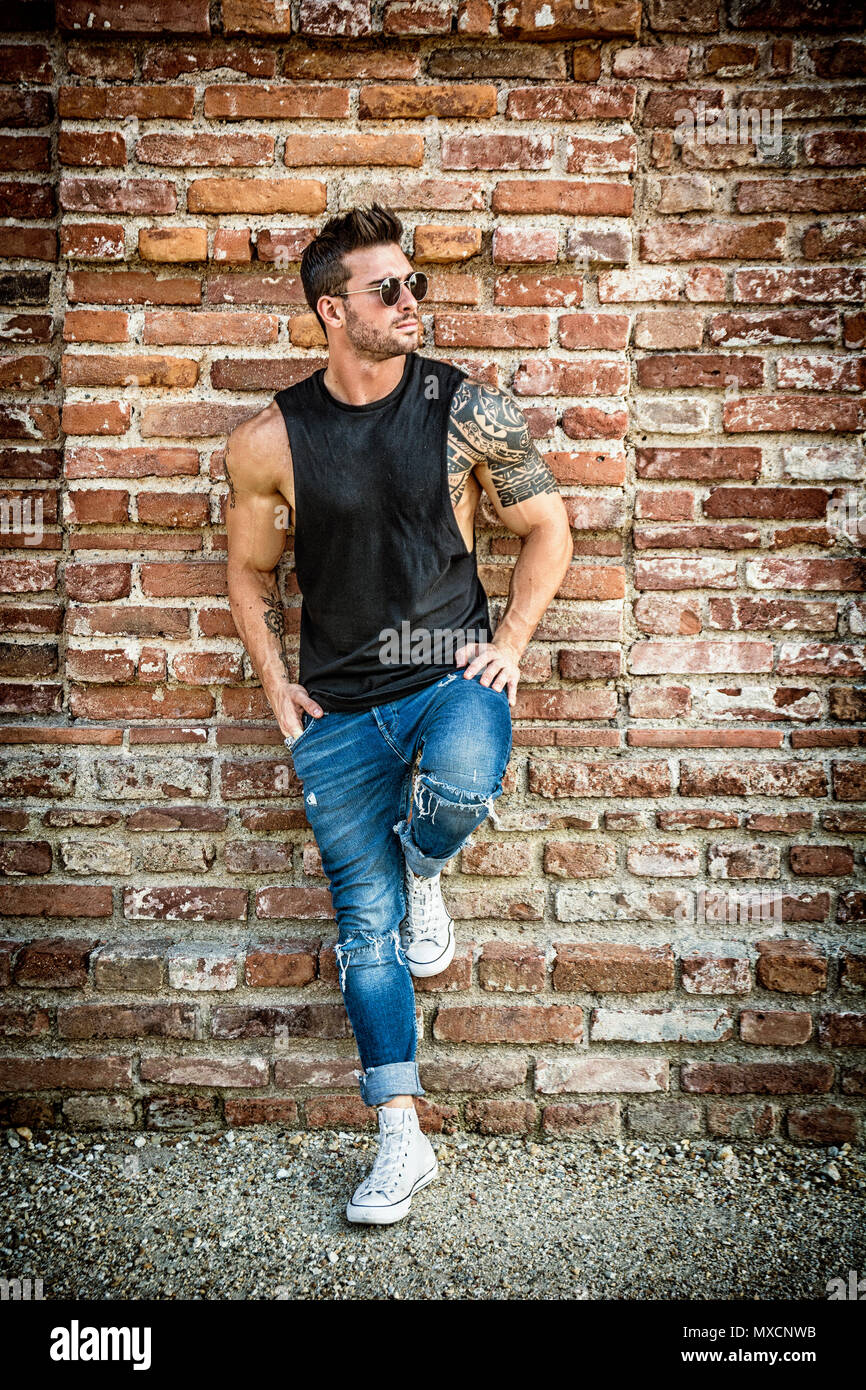 Muscular man leaning against old brick wall Stock Photo - Alamy