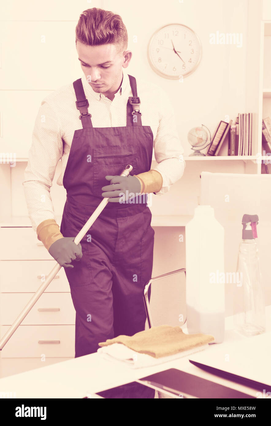 Diligent male professional janitor dusting in modern office interior ...