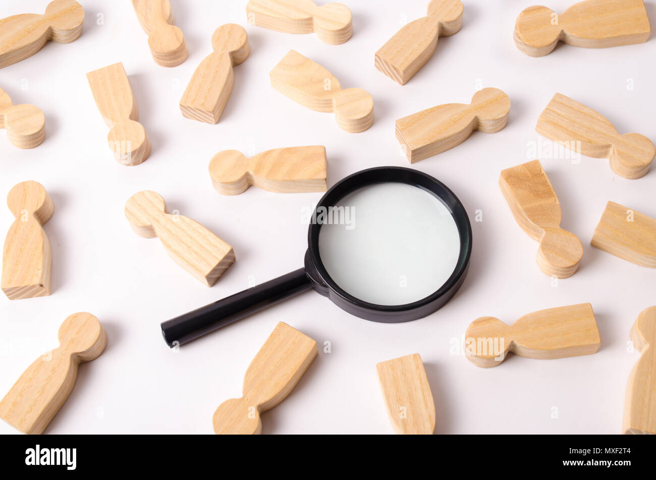 Wooden figures of people lie around a magnifying glass on a white ...
