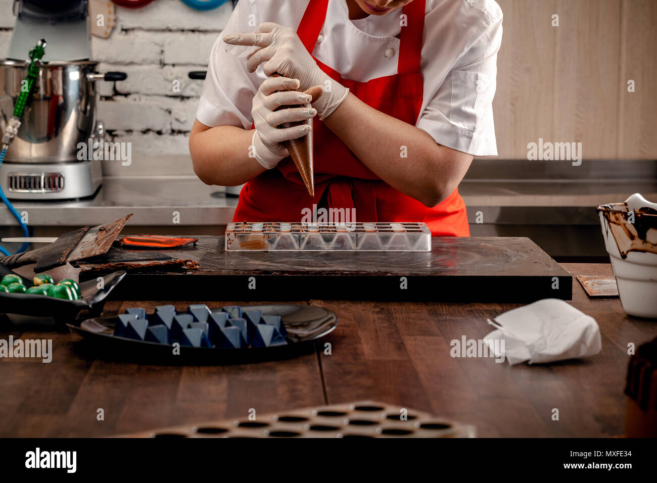 A woman confectioner with red uniform and white sterile gloves do a set ...
