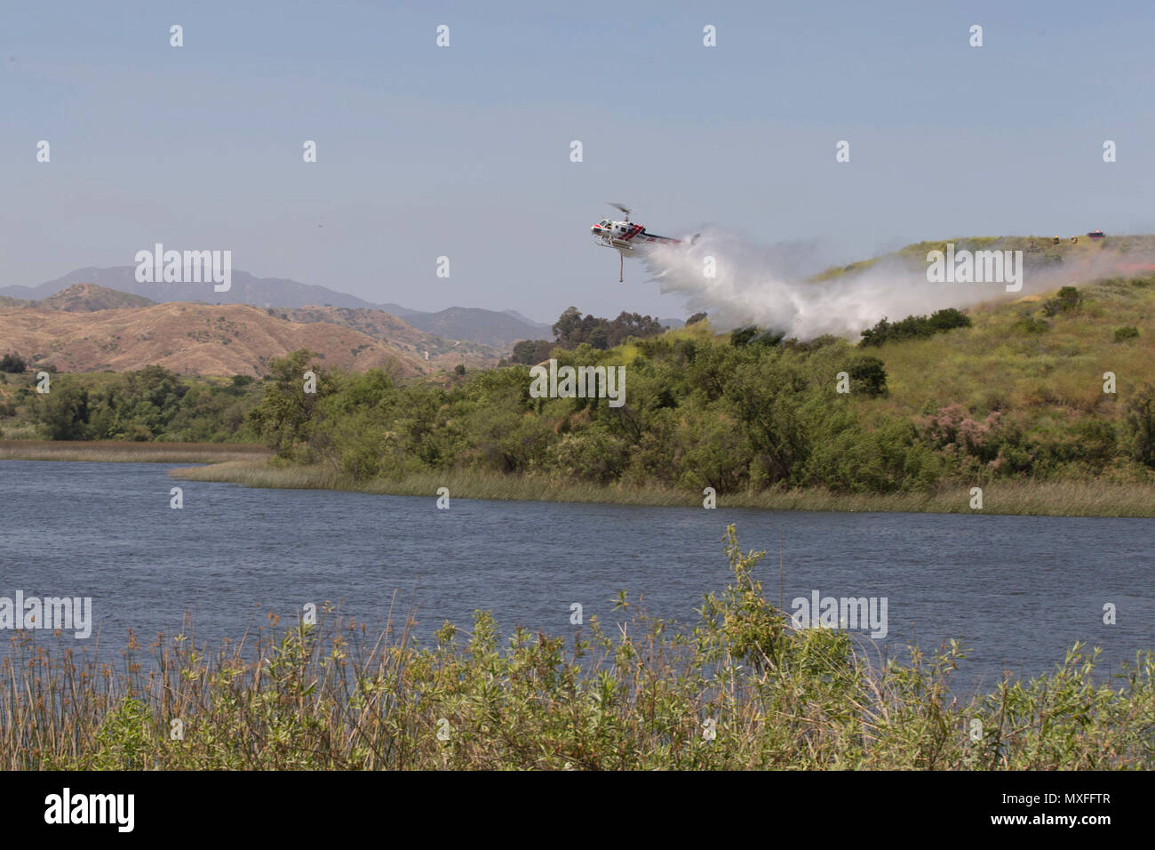 A CAL FIRE Bell 407 helicopter drops water on simulated fire area ...