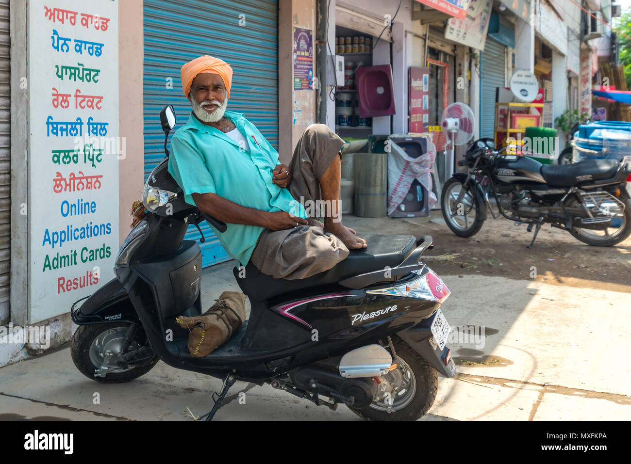An older man in a Sikh turban, is reclining on a motorcycle in front of ...