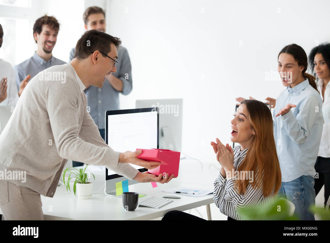 Diverse colleagues congratulating surprised female worker with g Stock ...