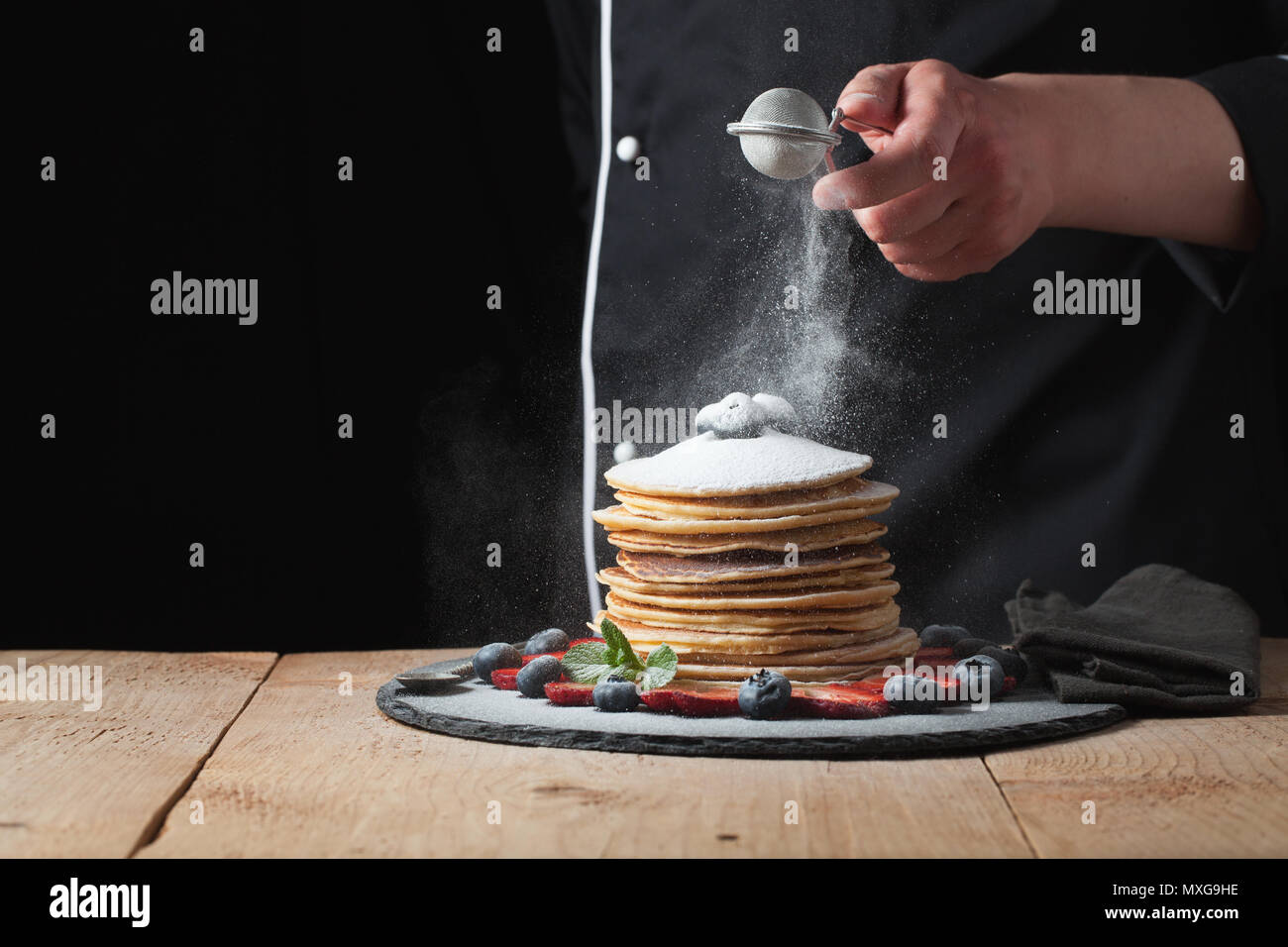 Serving pancakes with powdered sugar and berries. Chef woman hand ...