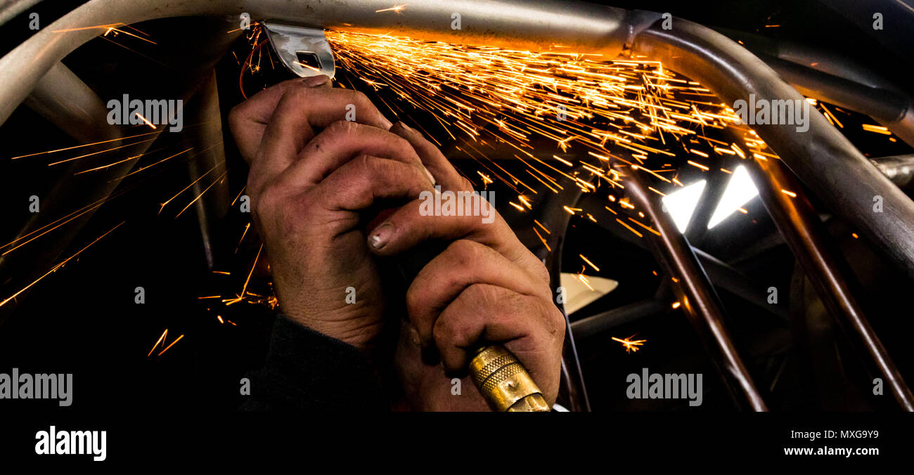 Man grinding steel tubing with a hot pneumatic grinding disc showering ...