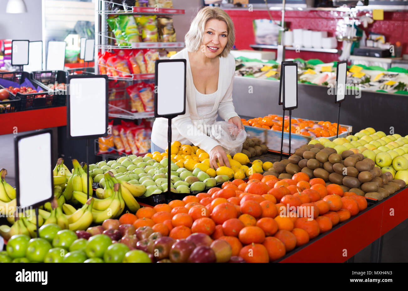 Mature woman choosing different fruits at farm food store display Stock ...