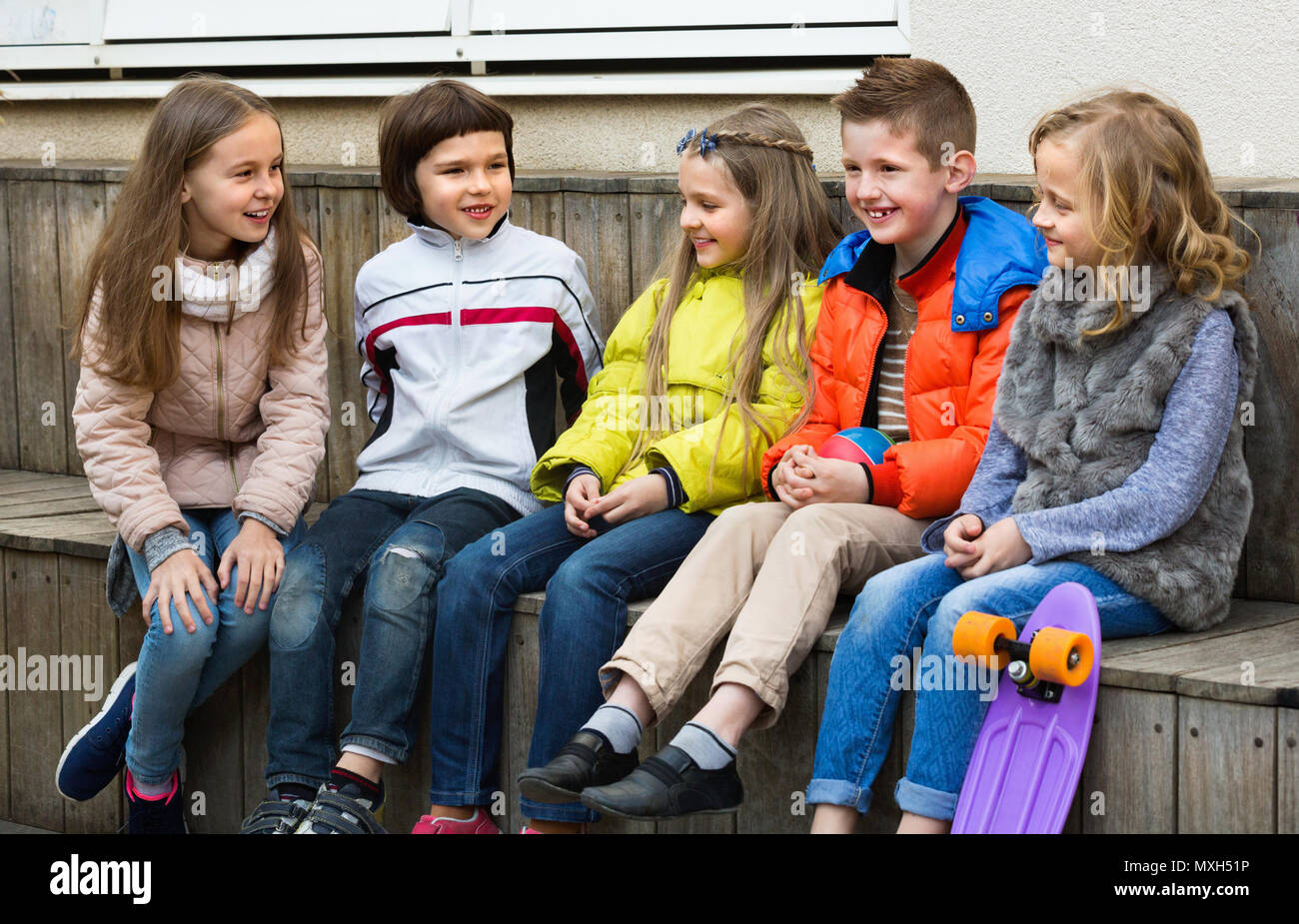 Group of positive children sitting on bench and sharing secrets ...