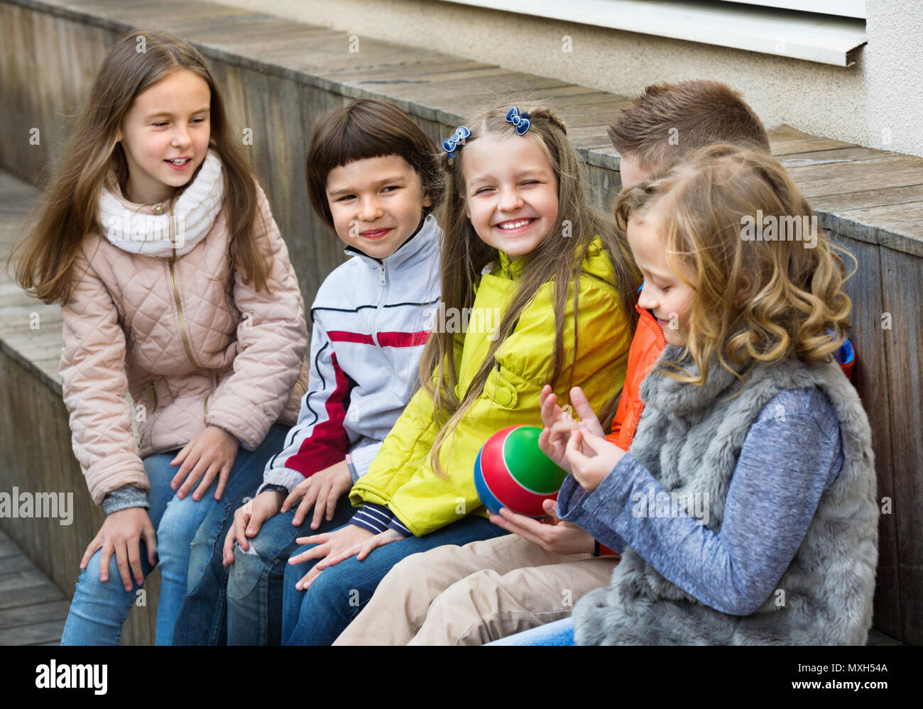 Group of cute children sitting on bench and sharing secrets outdoors ...