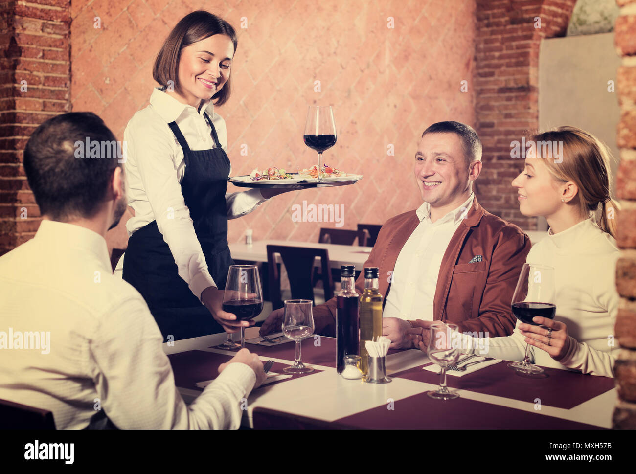 Happy young waitress placing order in front of guests in country ...
