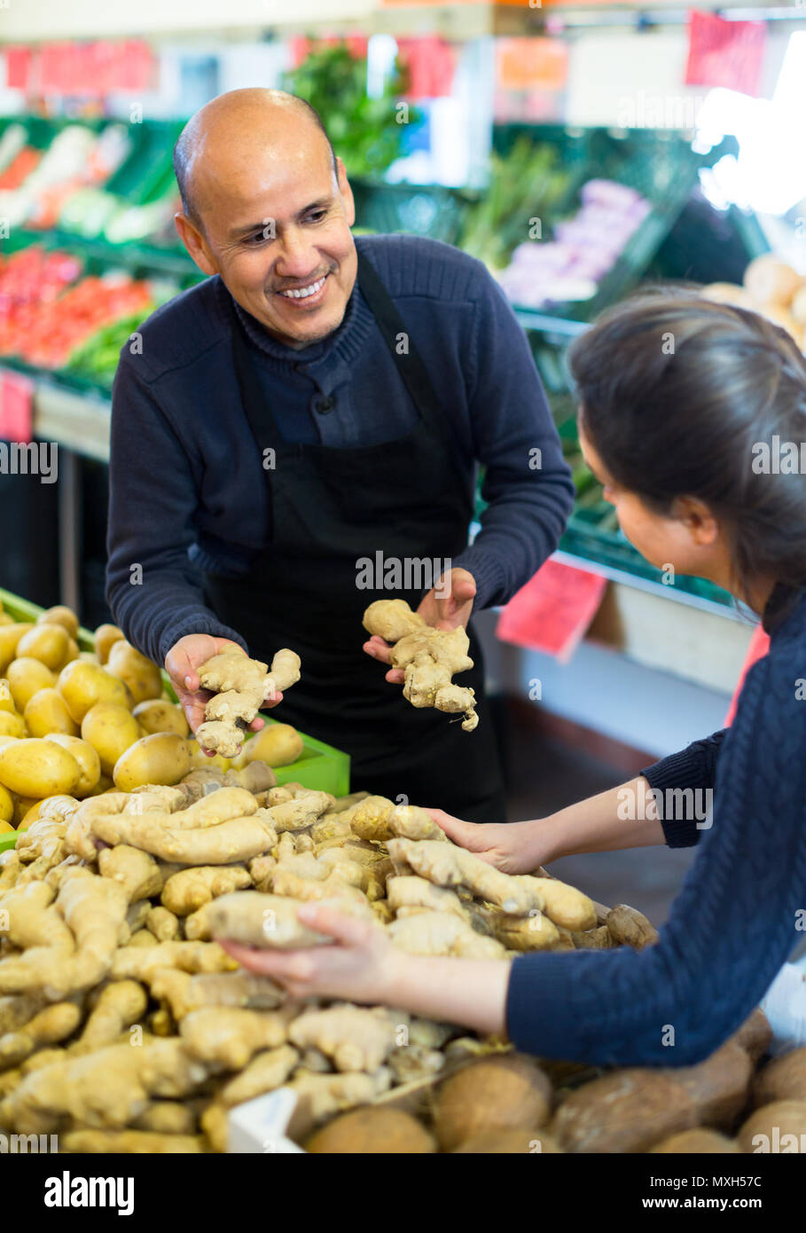 salesman helping female customer to choose ginger in supermarket Stock ...